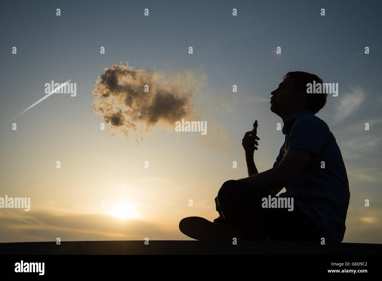 vaping young man with, produces vapor on sunset sky background at the ...