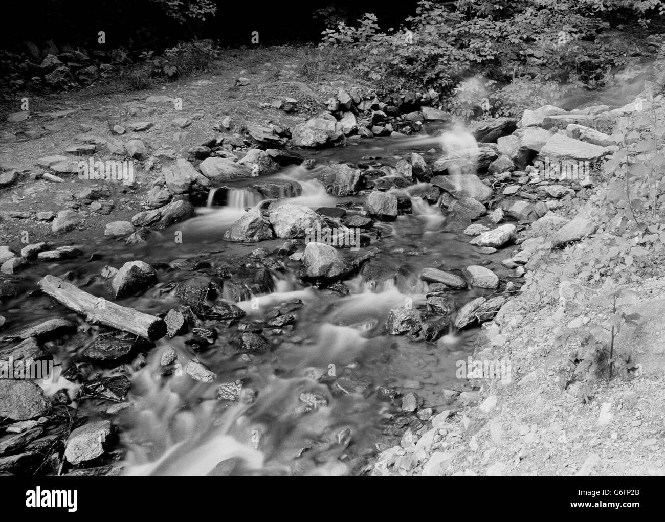 A slow shutter speed monochrome image of a stream with a young boy ...