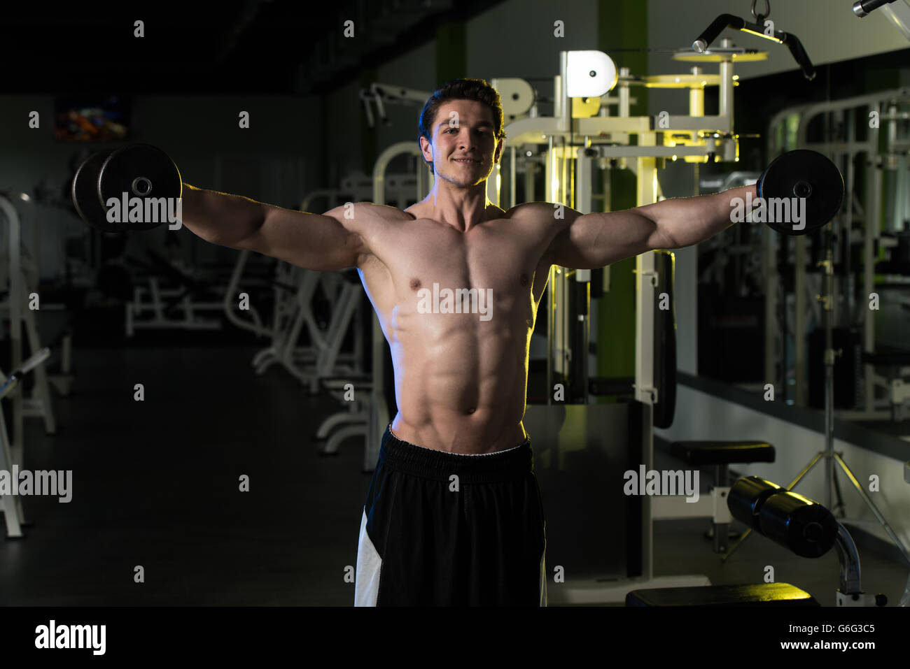 Young Man Working Out Shoulders In A Dark Gym - Bodybuilder Doing Heavy ...
