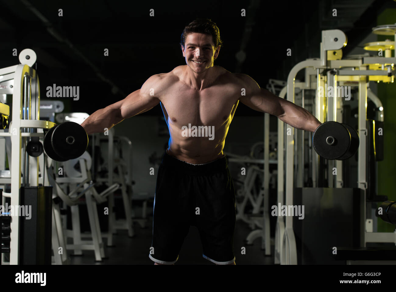 Young Man Working Out Shoulders In A Dark Gym - Bodybuilder Doing Heavy ...