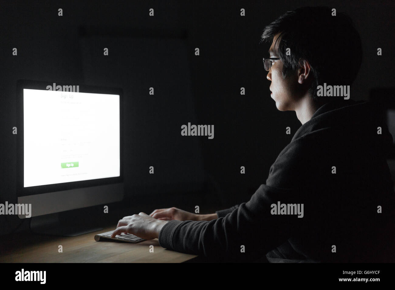 Serious young man sitting and working with computer in dark office ...