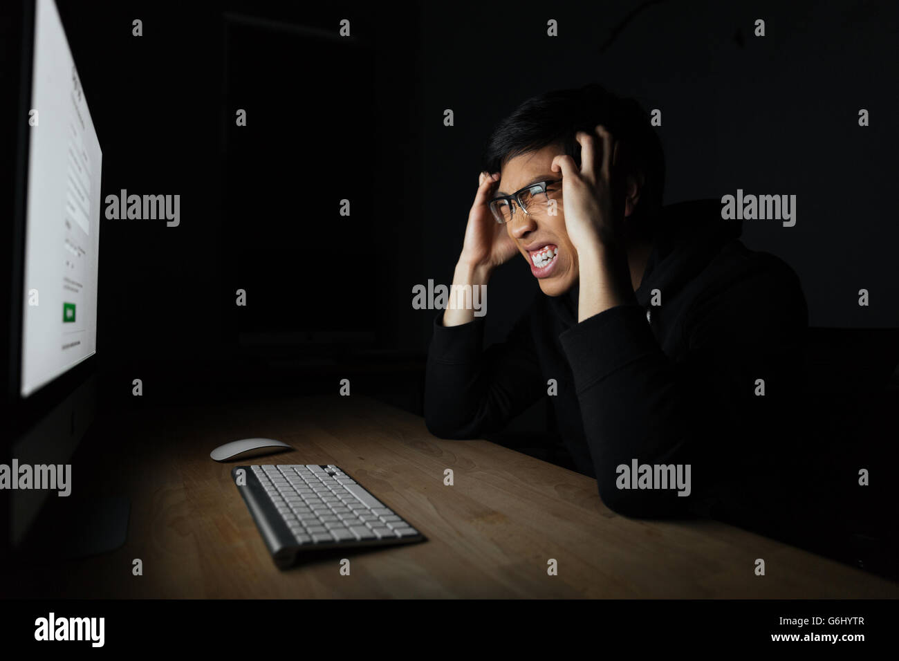 Mad irritated asian young man working with computer in dark room Stock ...