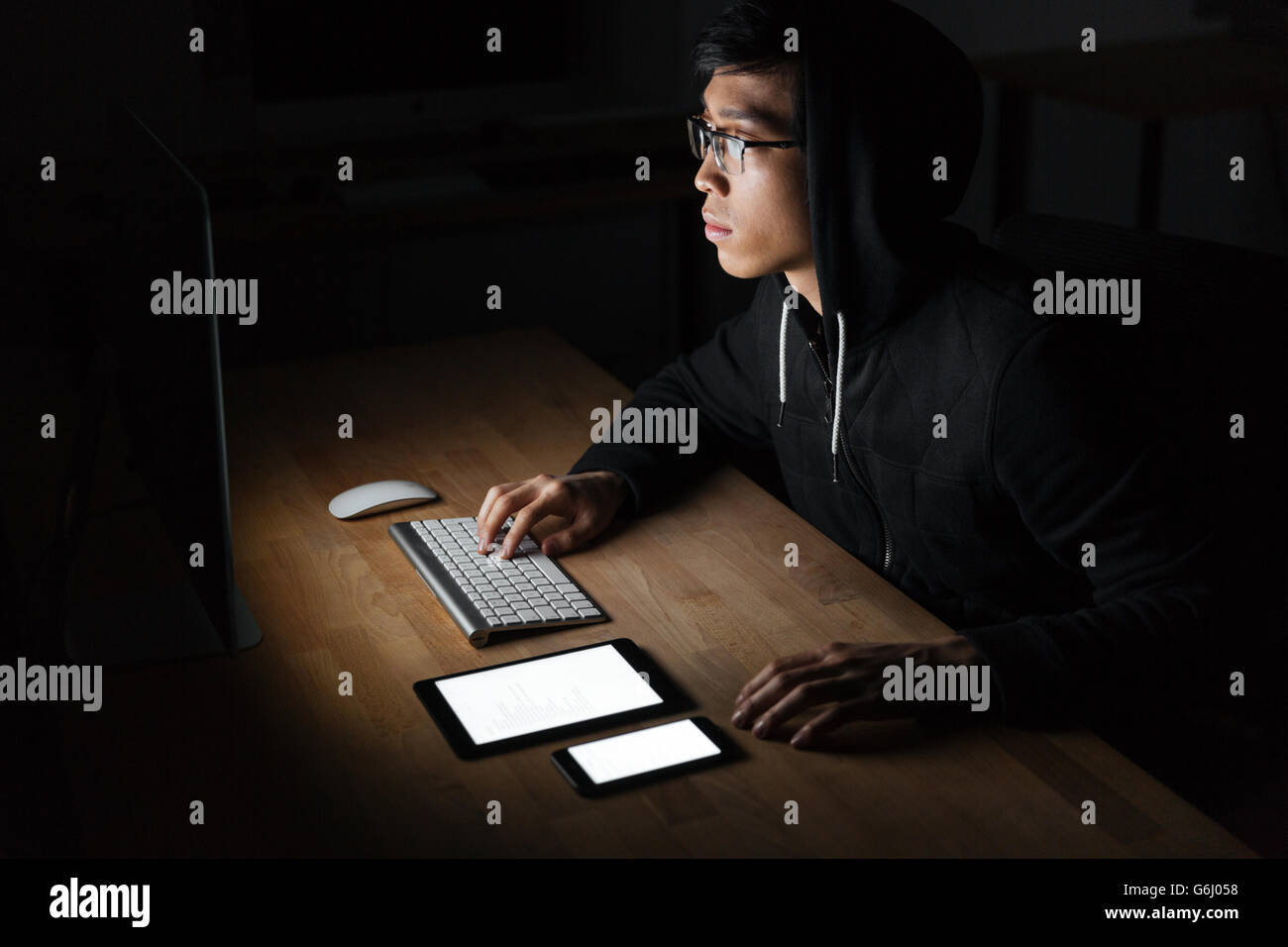 Hooded computer hacker stealing information using blank screen tablet ...