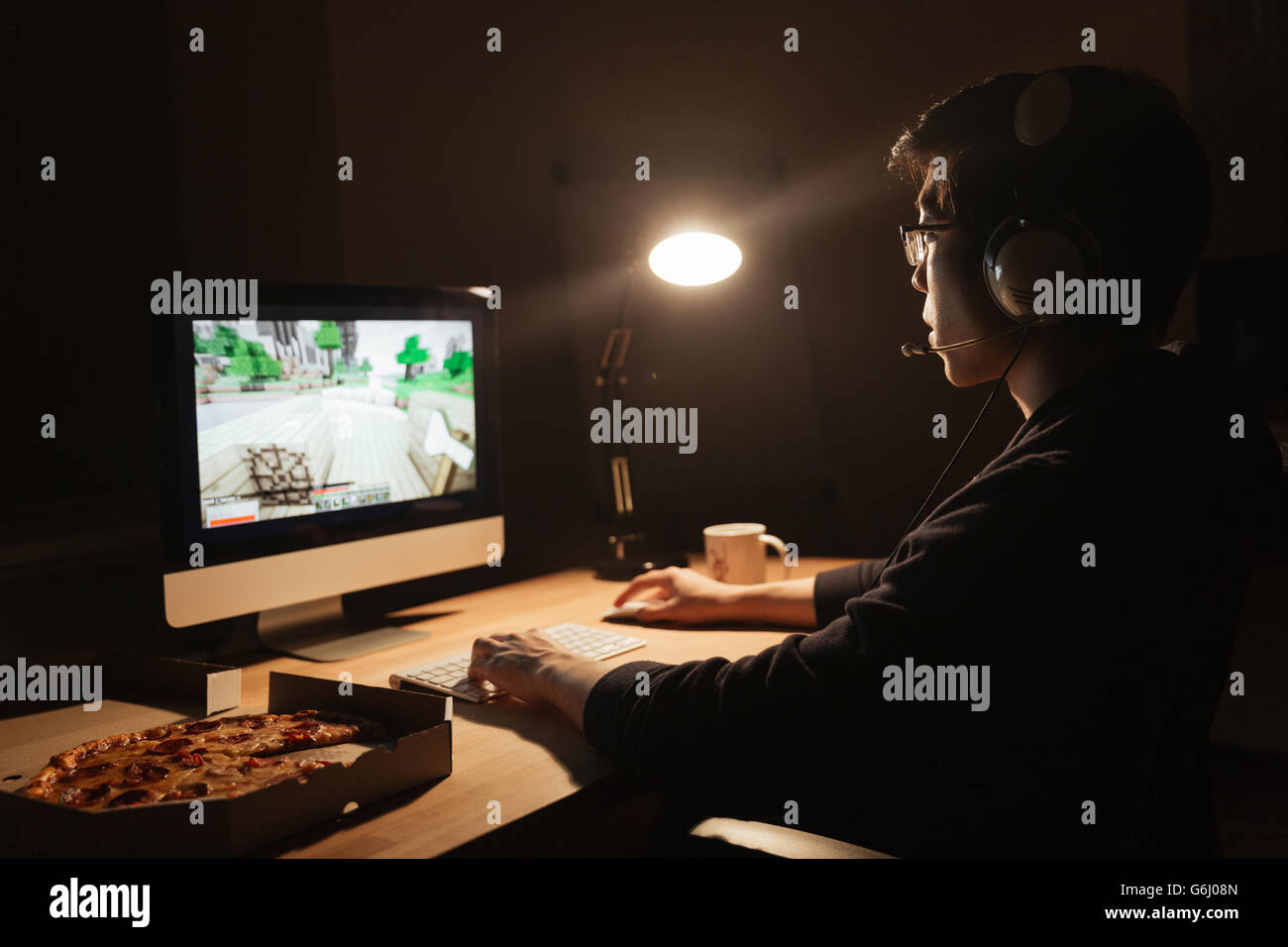 Man gamer in headset playing computer game and eating pizza in dark ...
