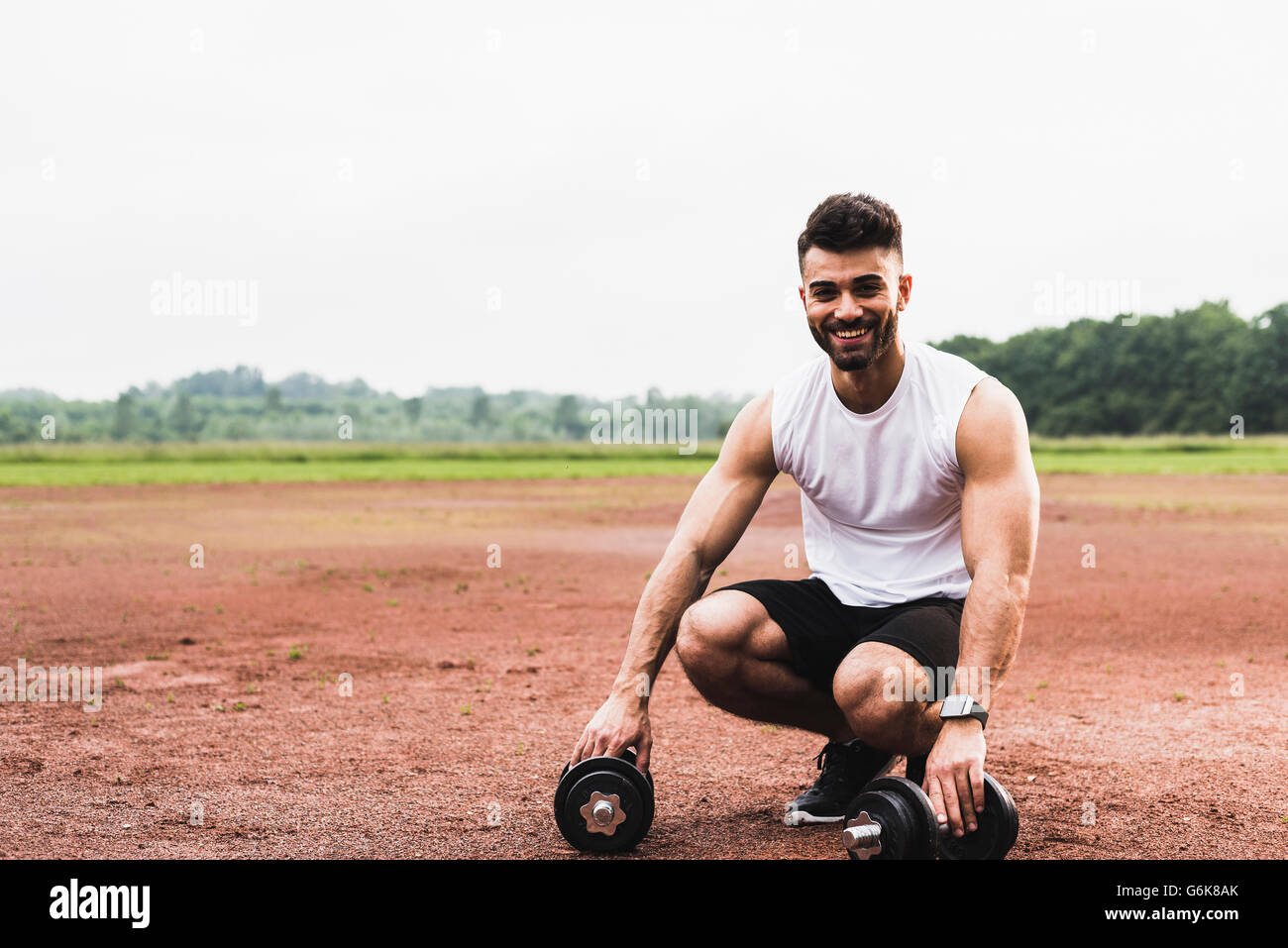 Portrait of smiling athlete with dumbbells on sports field Stock Photo ...