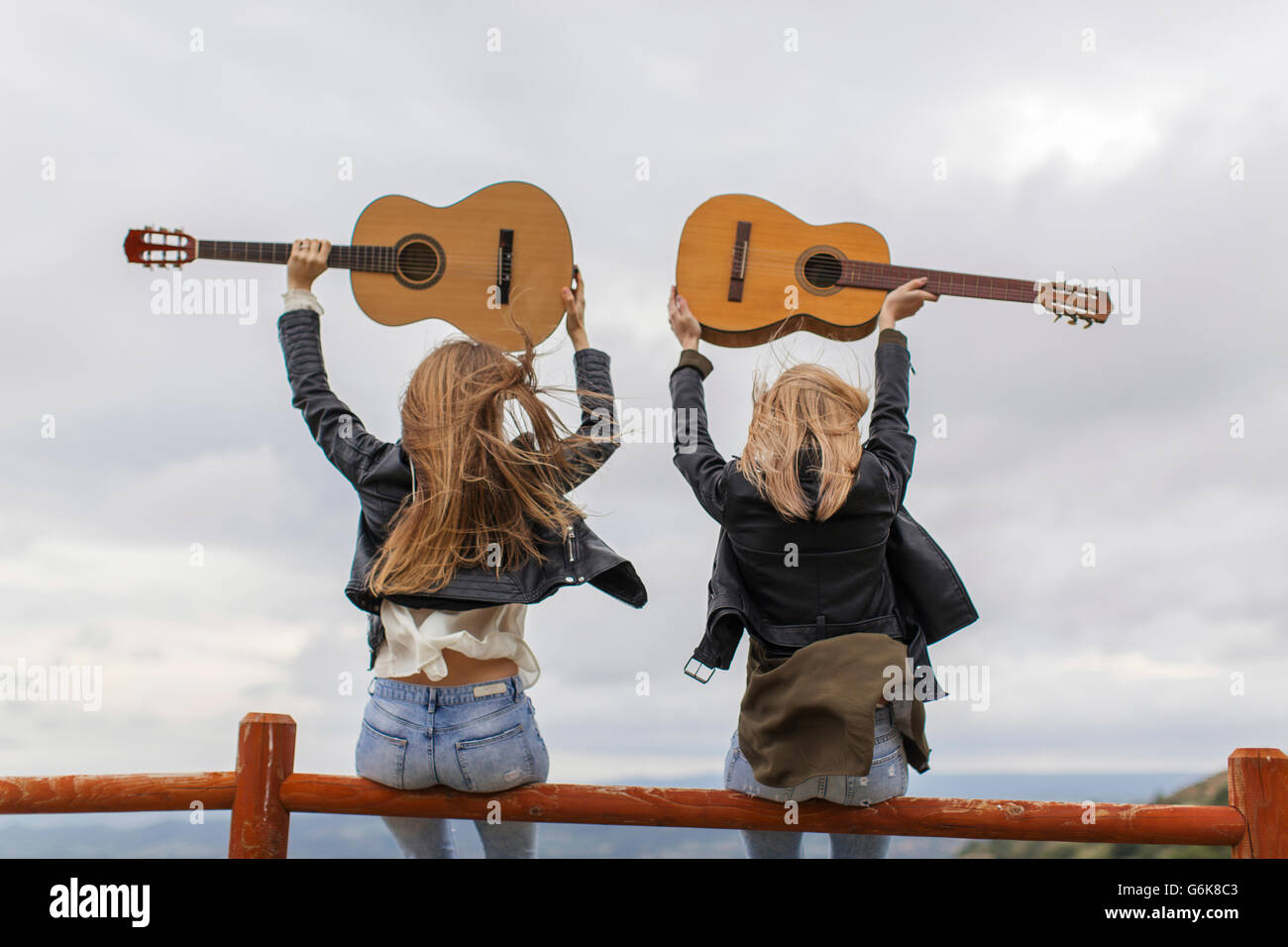 Two women sitting on wooden fence lifting up guitars Stock Photo - Alamy