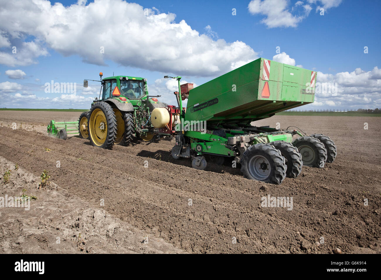 Farmer is planting dutch potatoes with his green tractor on his land ...