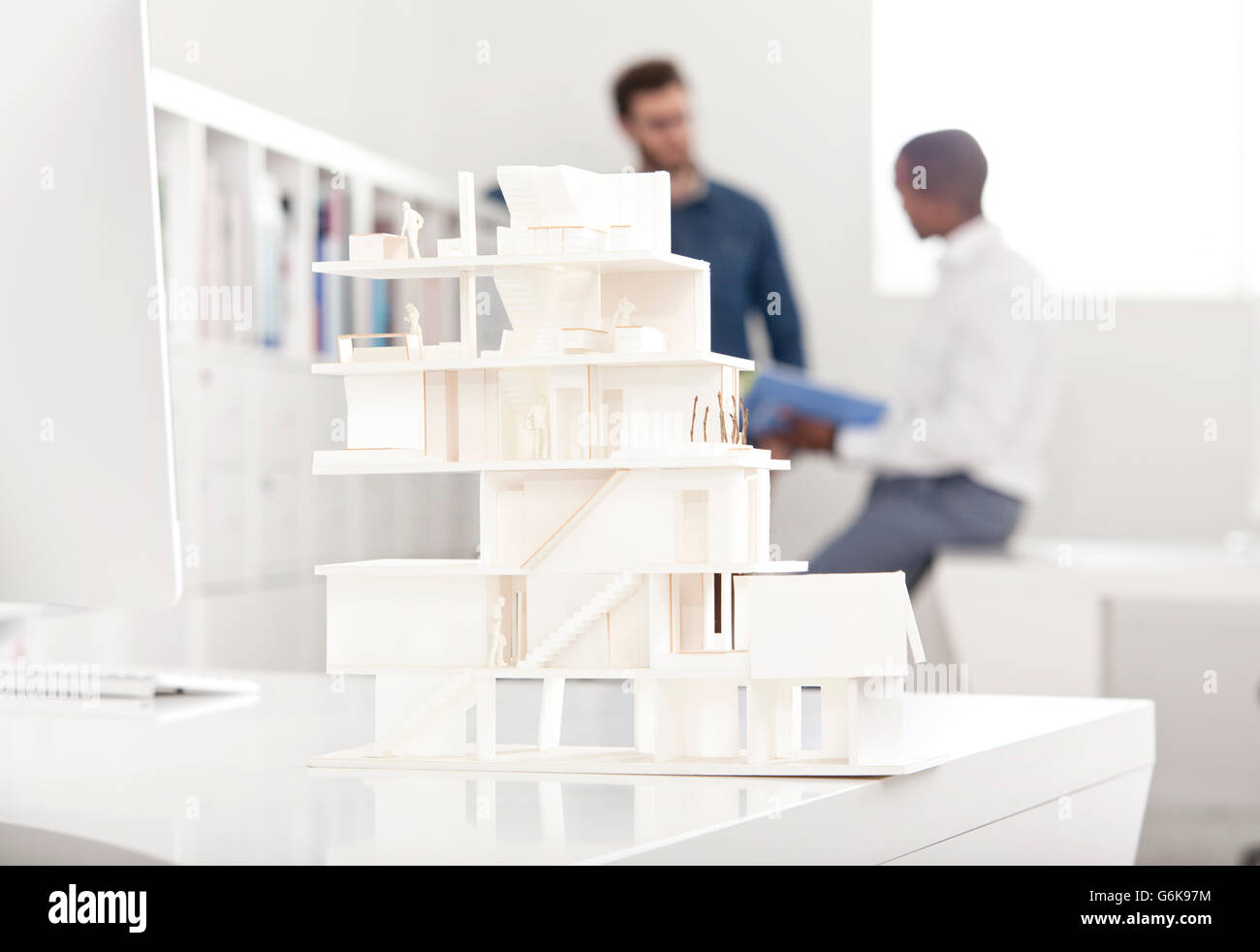 Architectural model on desk in an office with two talking people in the ...