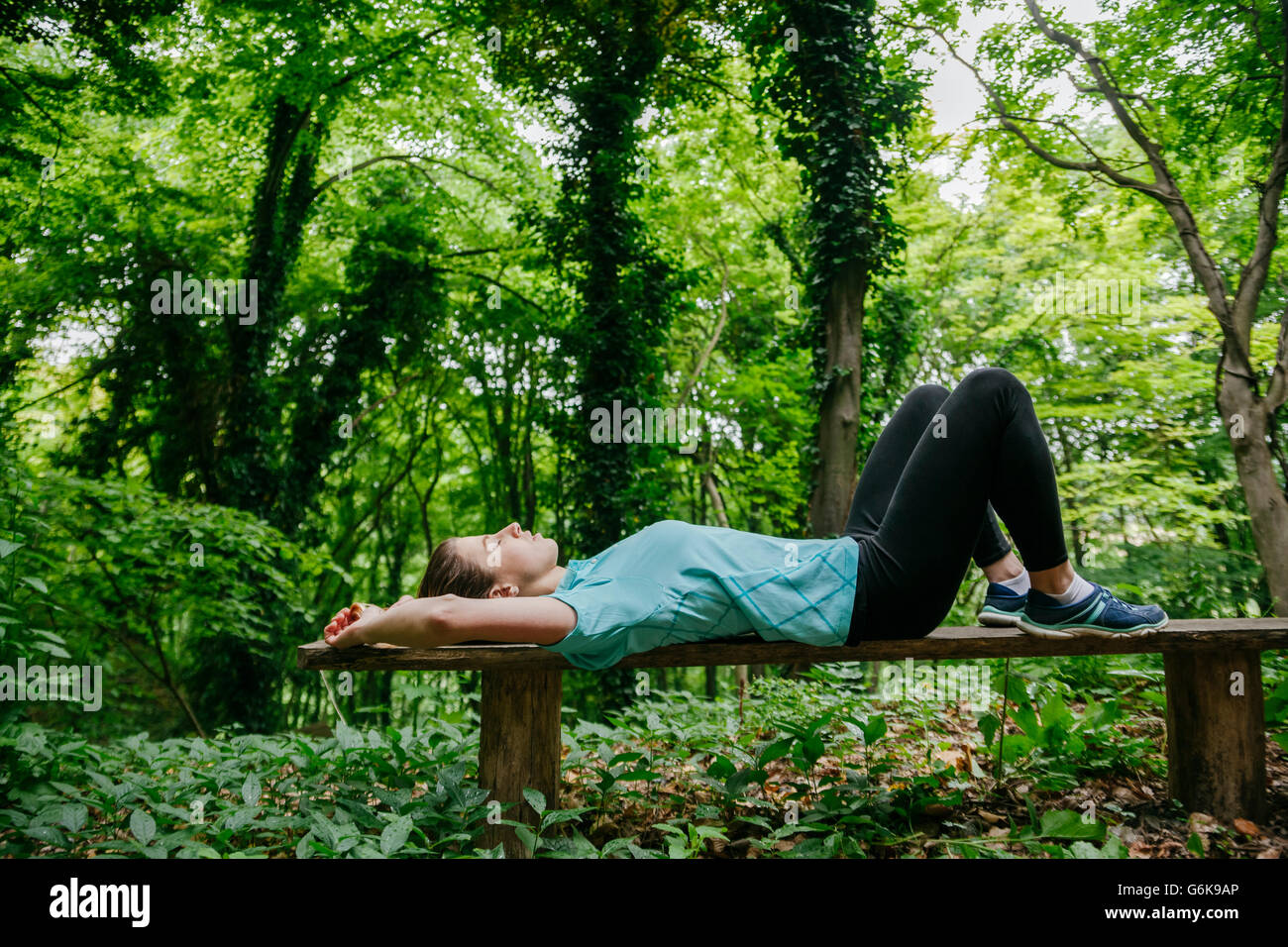 Young woman relaxing on bench in forest Stock Photo - Alamy
