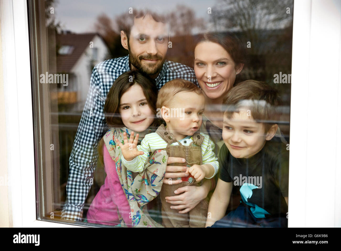 Happy family of five looking through window pane Stock Photo - Alamy