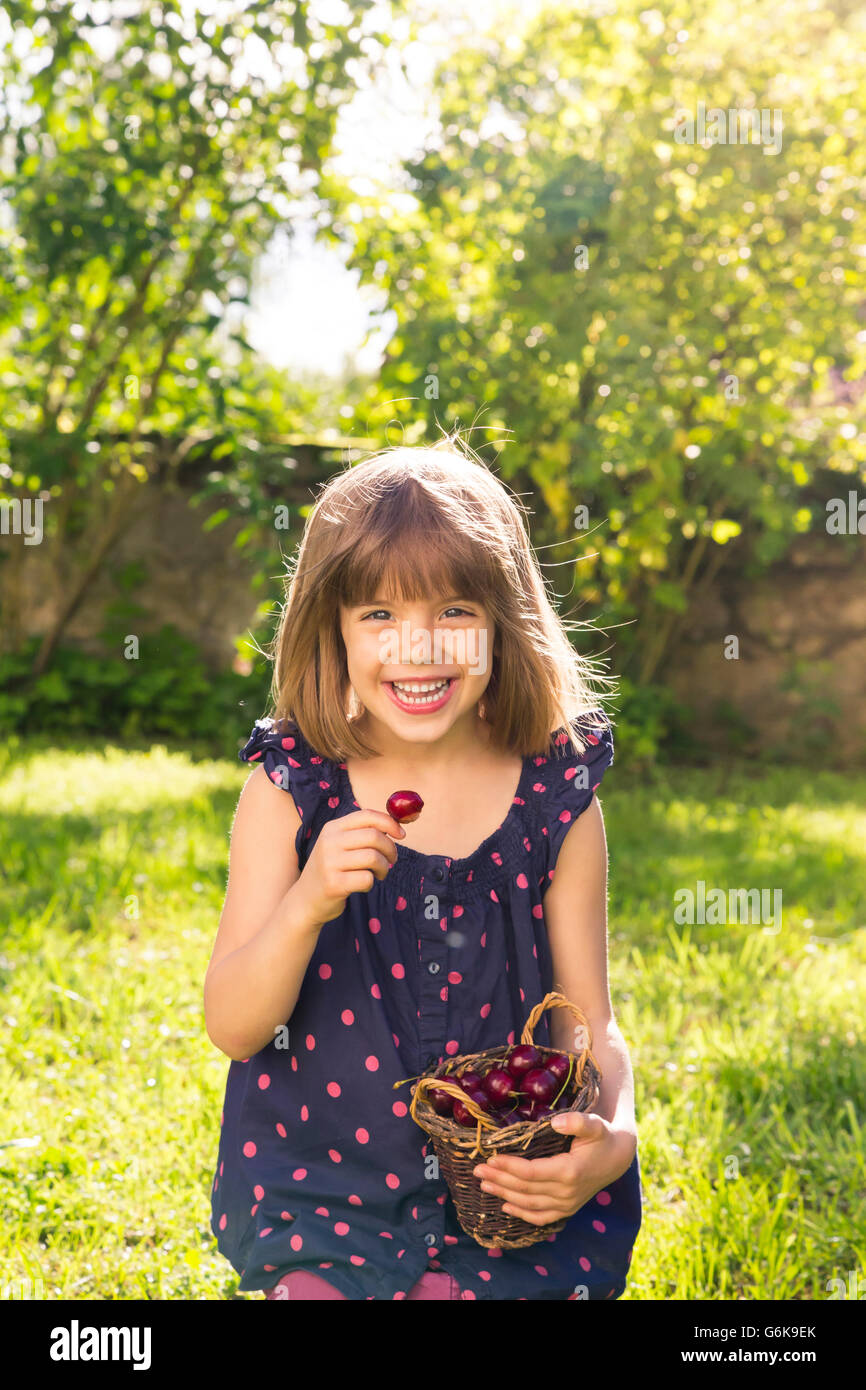 Portrait of laughing little girl eating cherries in the garden Stock ...