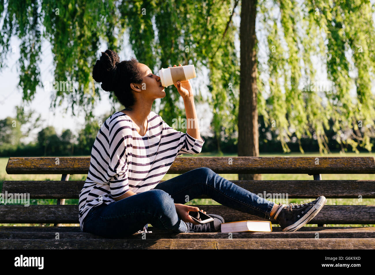 Young woman sitting on park bench drinking coffee to go Stock Photo - Alamy