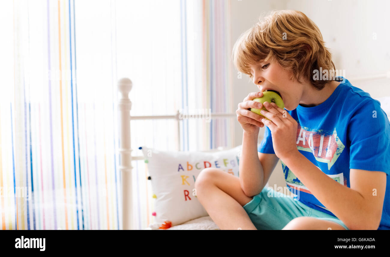 Portrait of boy sitting on the couch eating an apple Stock Photo - Alamy