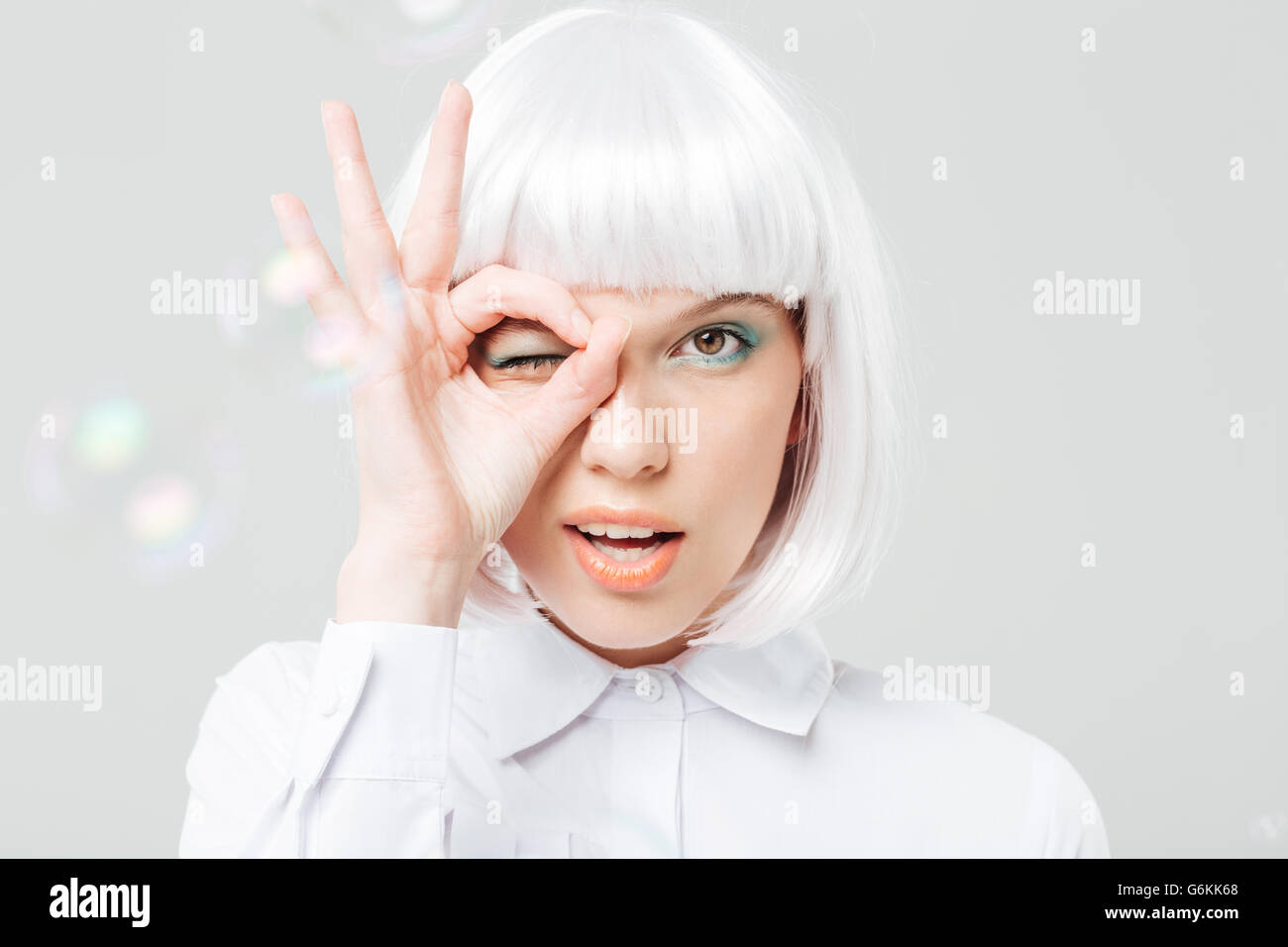 Playful charming young woman looking through her fingers over white ...