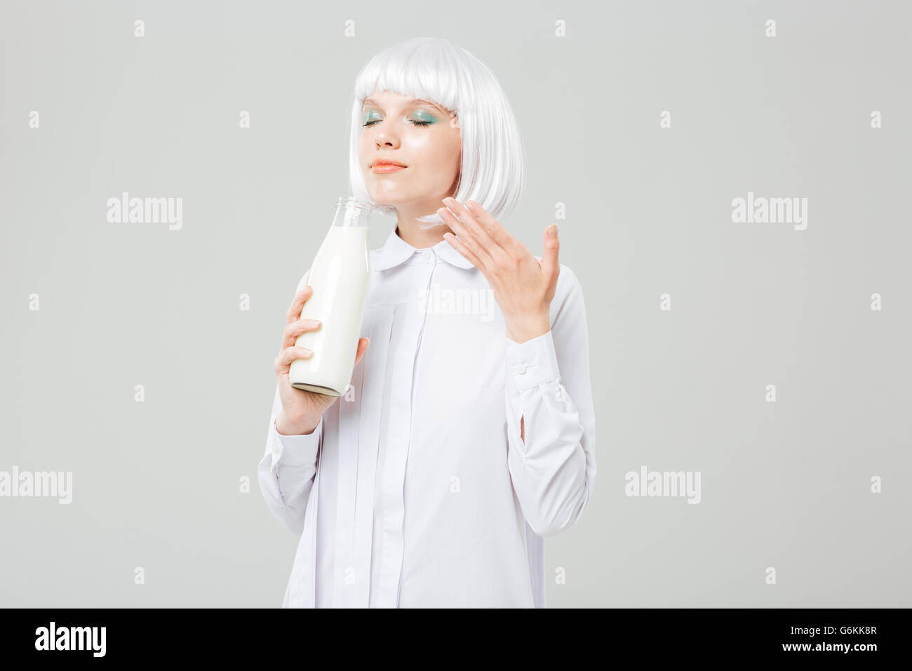 Attractive inspired young woman smelling milk in bottle over white ...