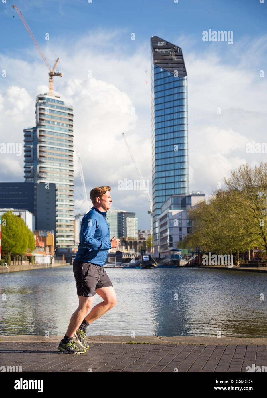 Young man jogging on early evening run with office blocks in background ...