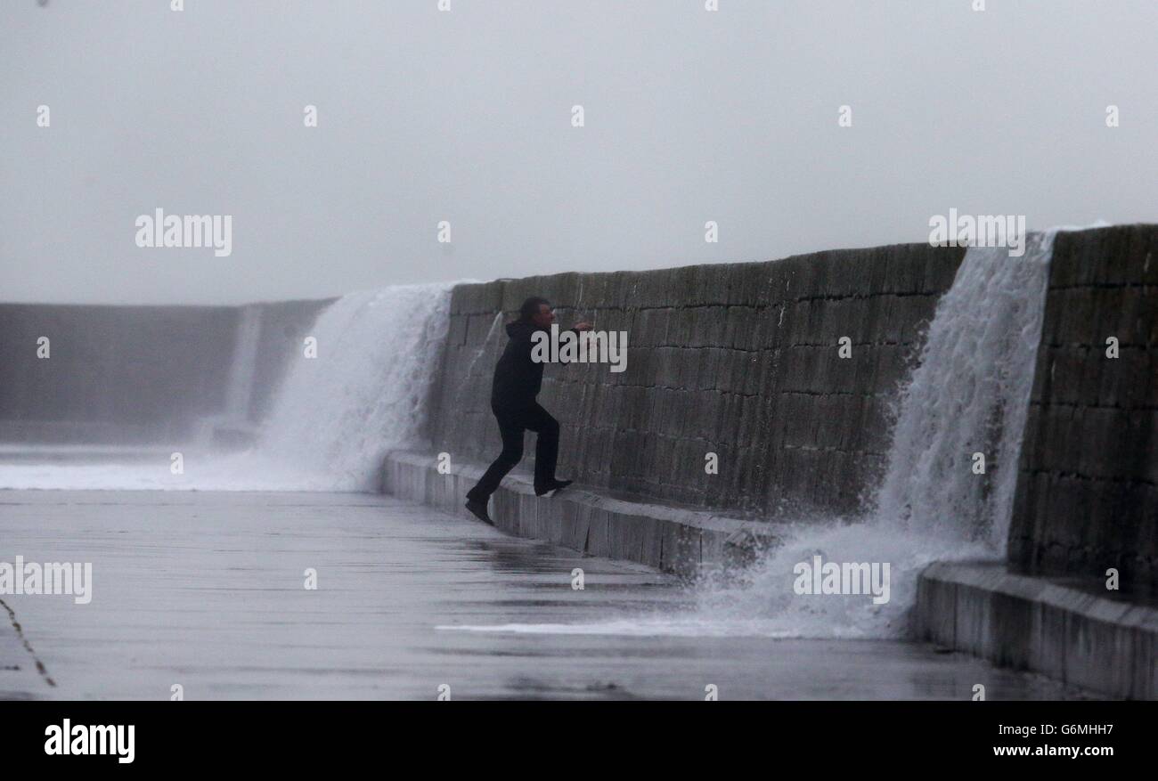 A looks over the wall as wave crashing onto the East pier in Howth ...