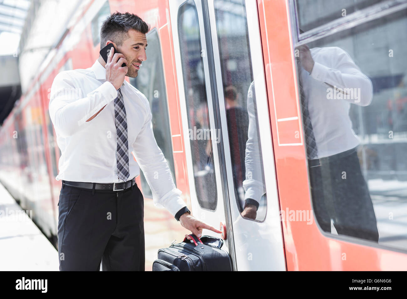 Businessman on cell phone getting into train Stock Photo - Alamy