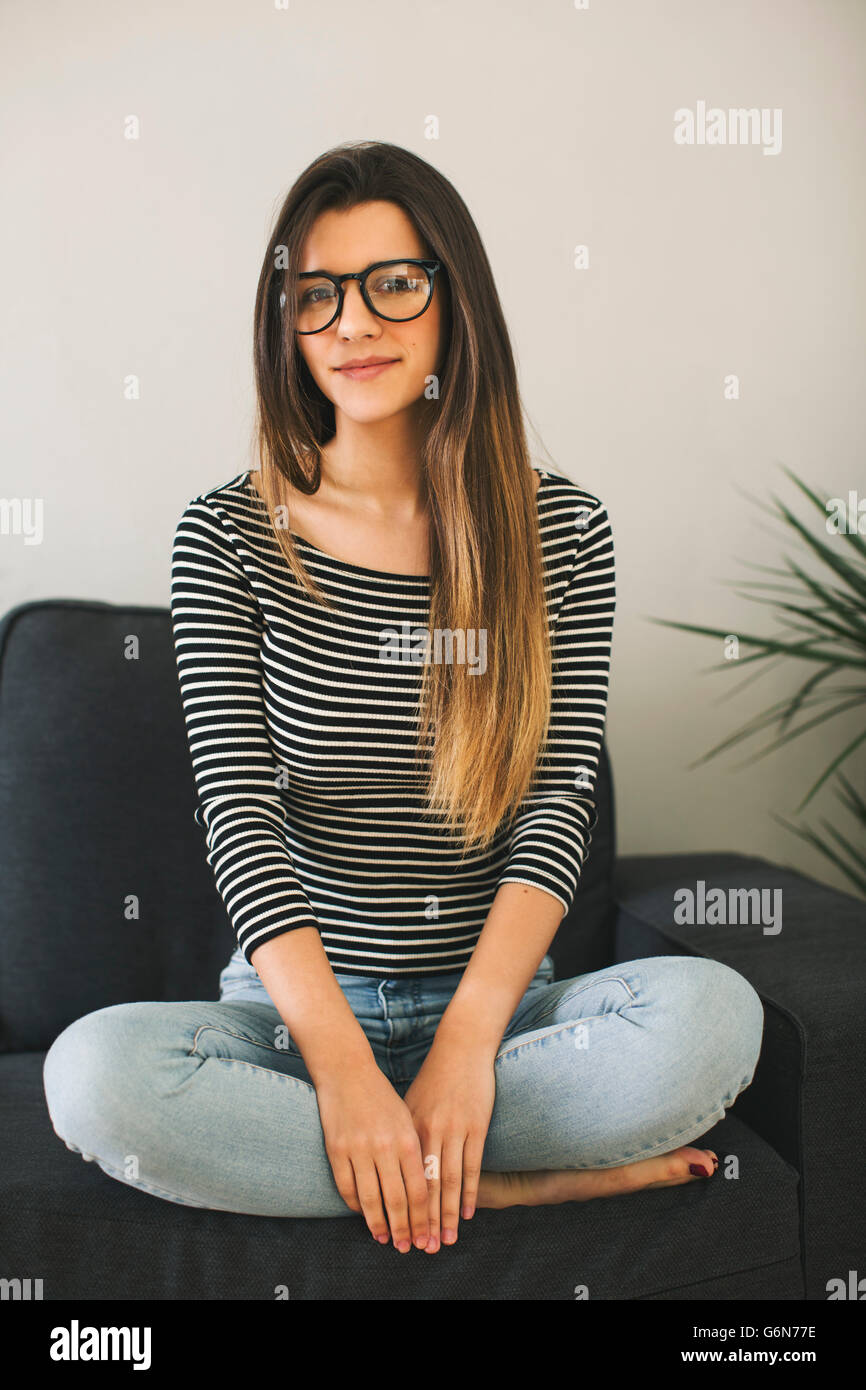Young woman sitting cross-legged on couch Stock Photo - Alamy