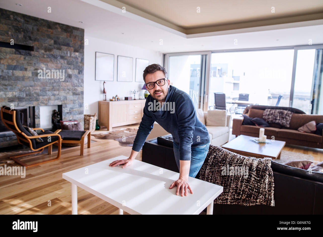 Man standing in living room, leaning on desk Stock Photo - Alamy