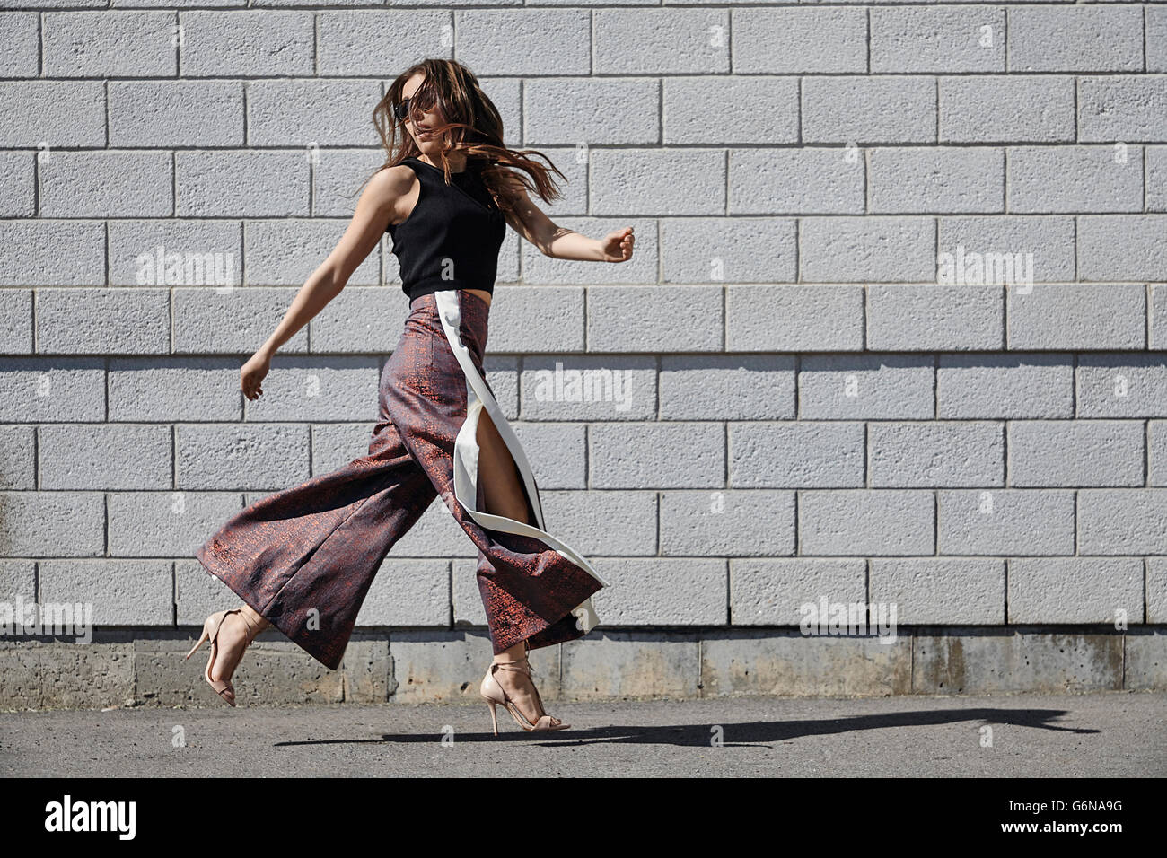 Fashionable young woman passing brick wall Stock Photo - Alamy