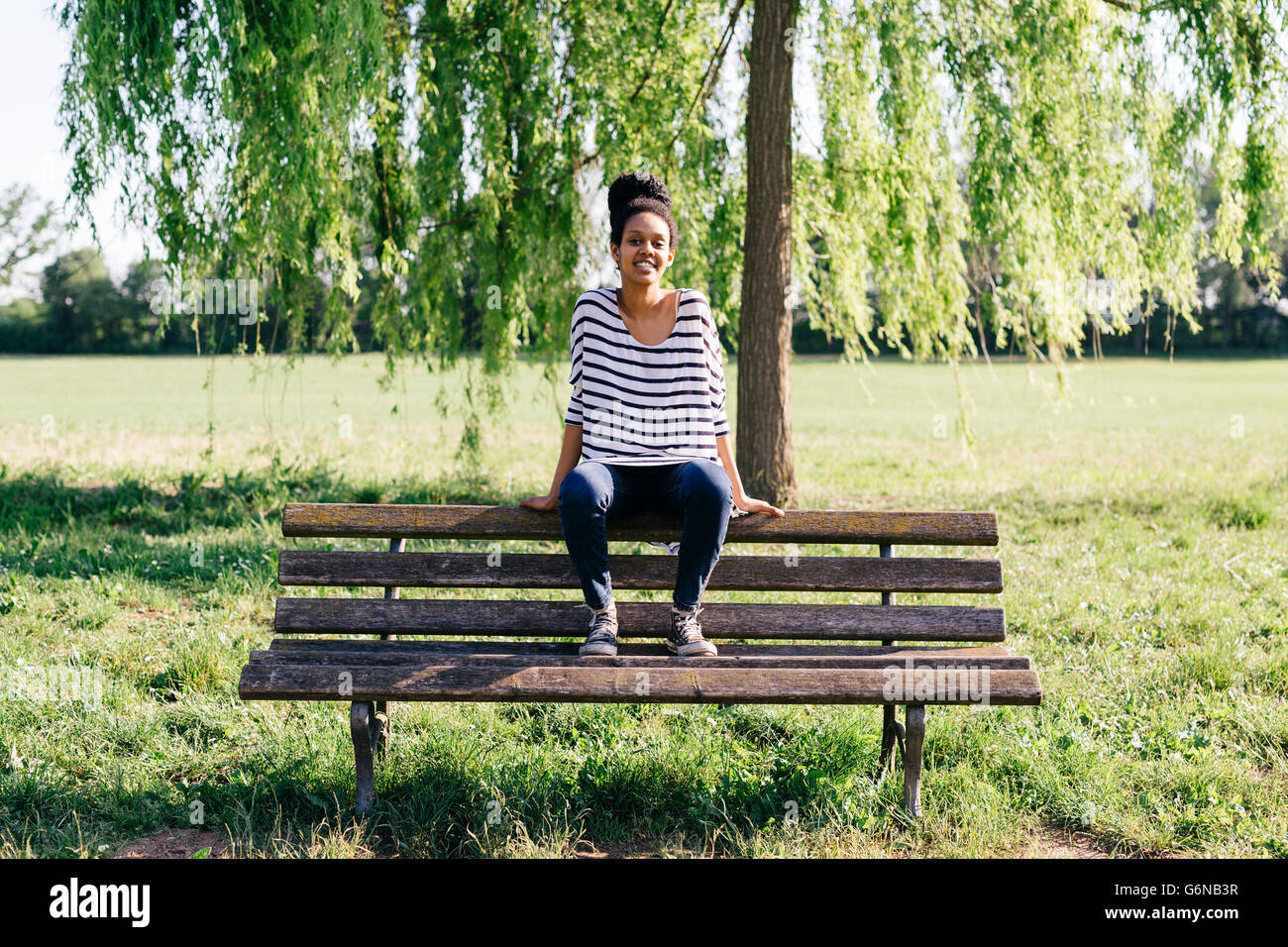 Portrait of young woman sitting on backrest of park bench Stock Photo ...