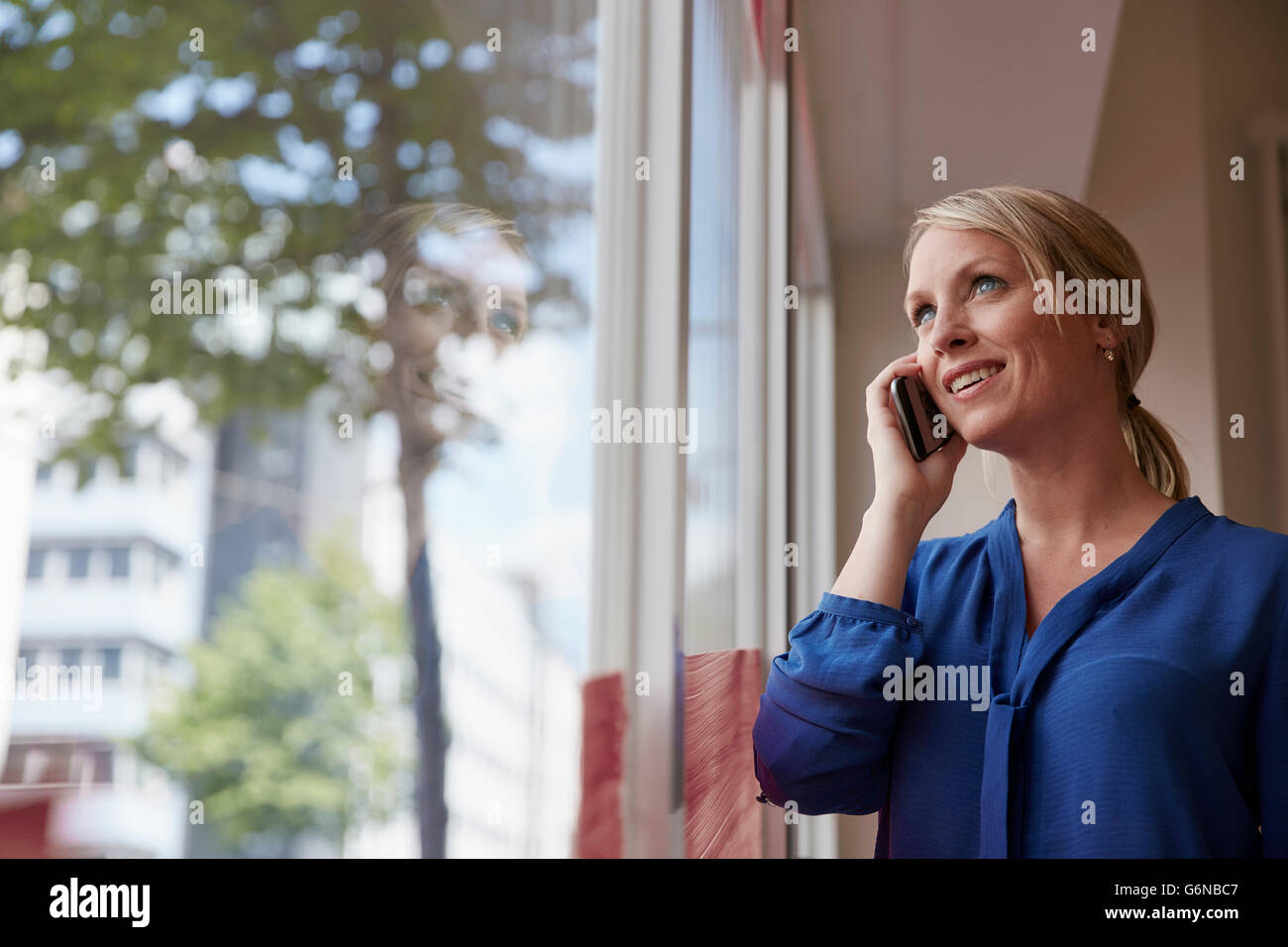 Businesswoman standing by window, talking on the phone Stock Photo - Alamy