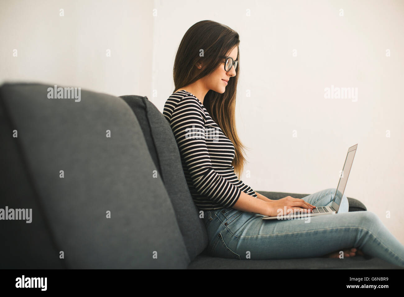 Young woman sitting on couch using laptop Stock Photo - Alamy