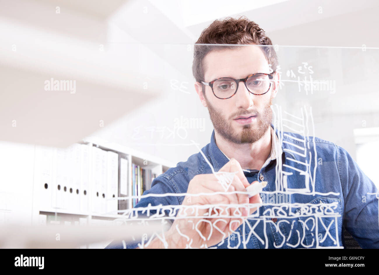 Portrait of young man drawing on glass pane in an office Stock Photo ...