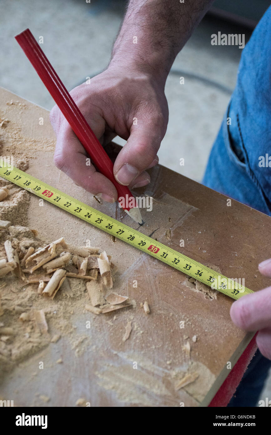 Hands of a carpenter measuring a wood plank with a tape measure and ...