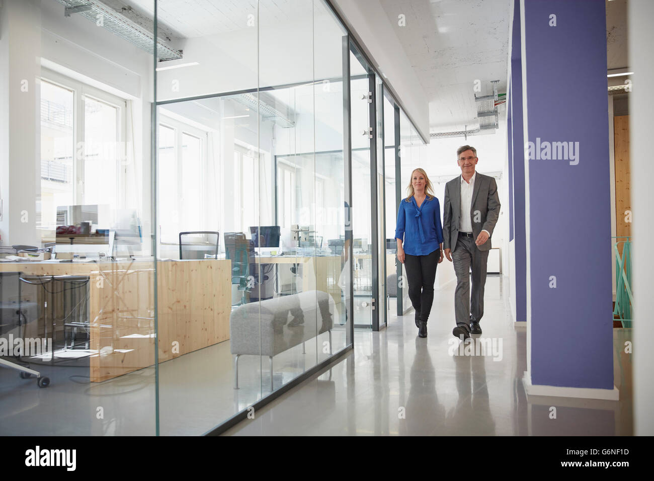 Businessman and woman walking down office corridor Stock Photo - Alamy