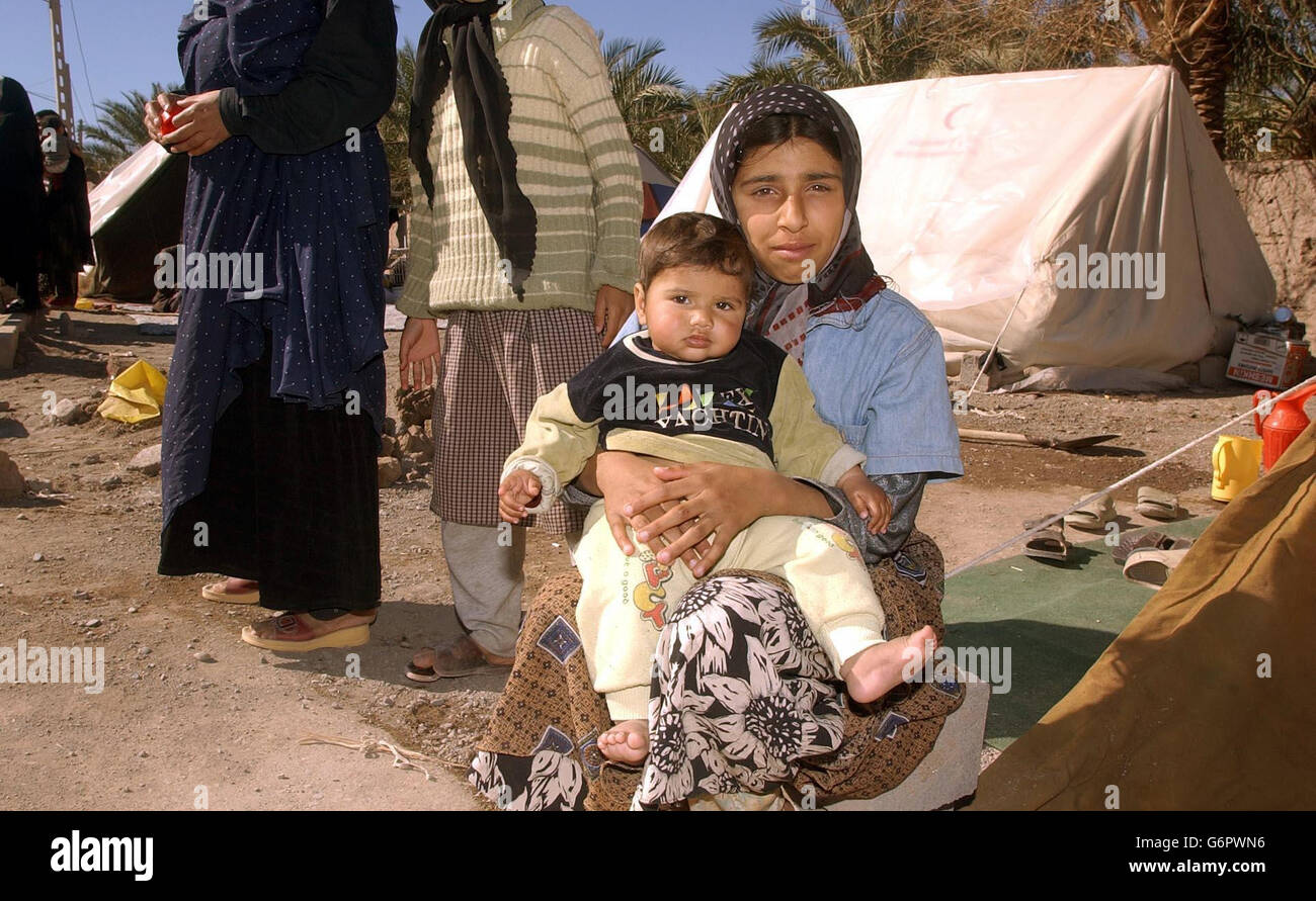 A young Iranian mother and her baby sit outside their tent, and watch ...