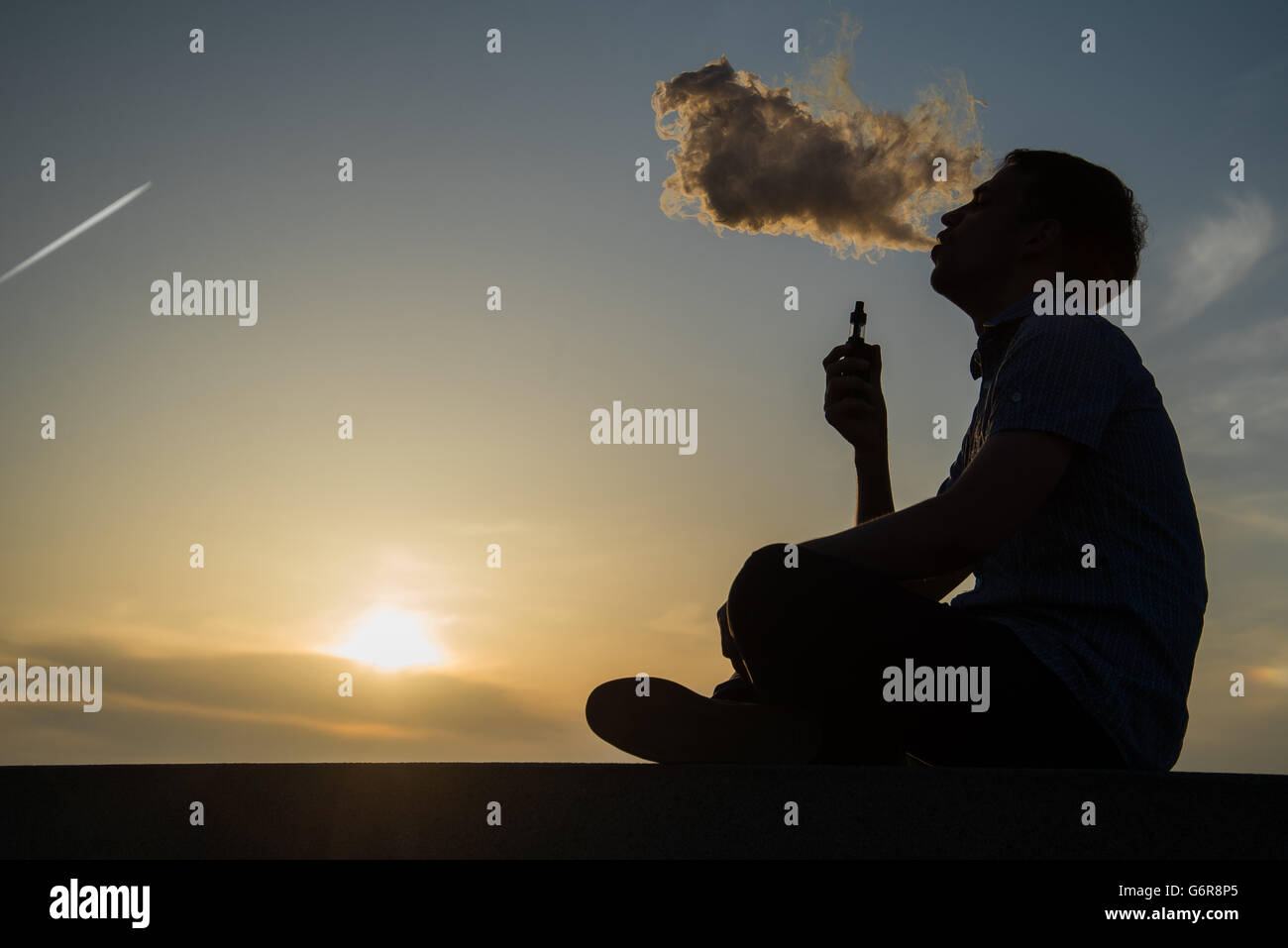 vaping young man with, produces vapor on sunset sky background at the ...