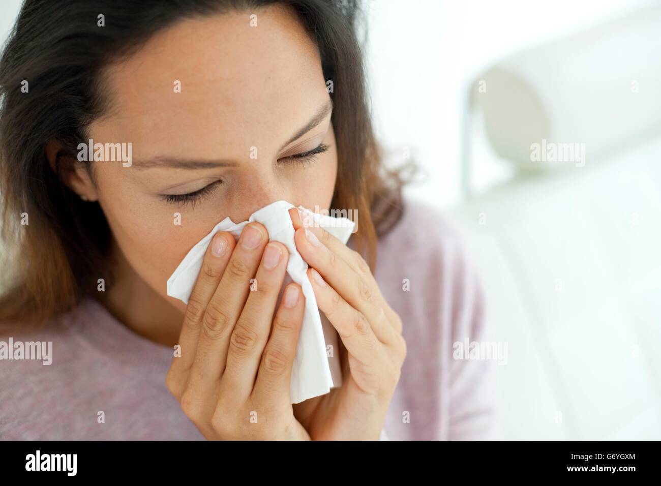 MODEL RELEASED. Young woman with a cold blowing her nose on a tissue ...