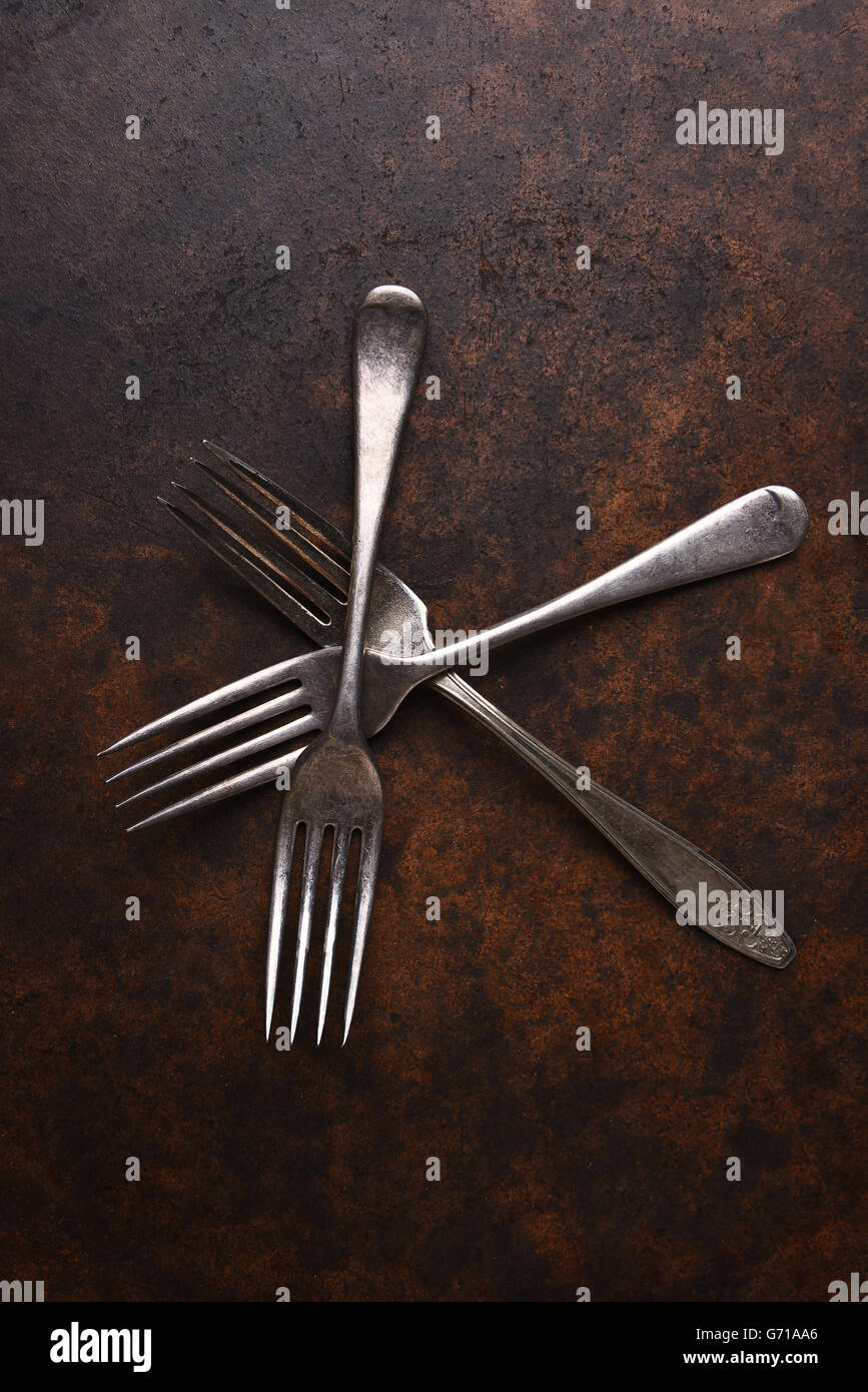Top view of a group of old forks on a dark mottled surface. Vertical ...