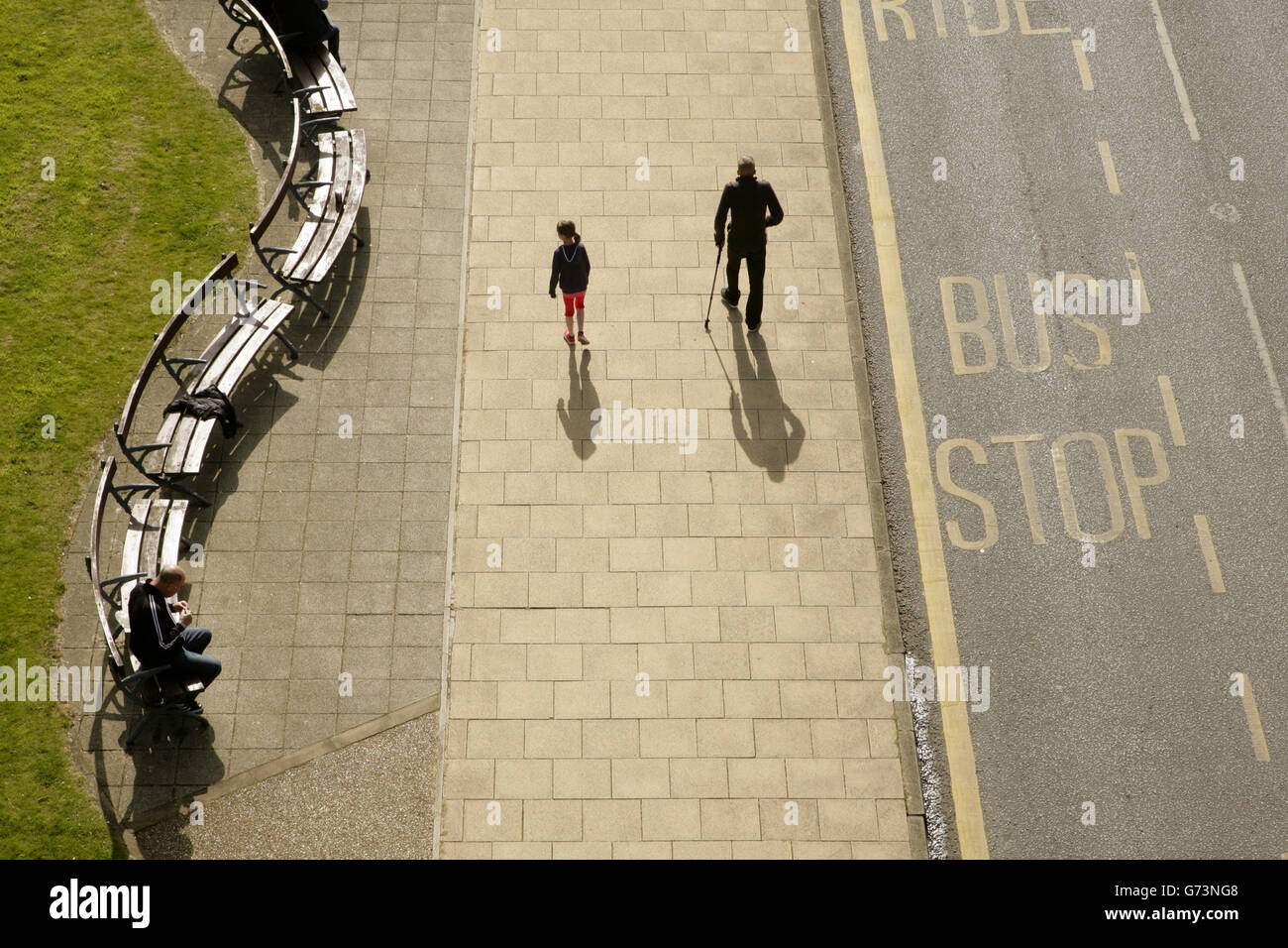 Man sitting on curved wooden bench at an empty bus stop while man and ...