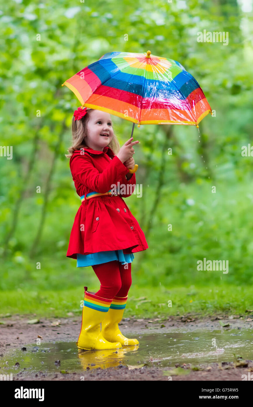 Little girl playing in rainy summer park. Child with colorful rainbow ...