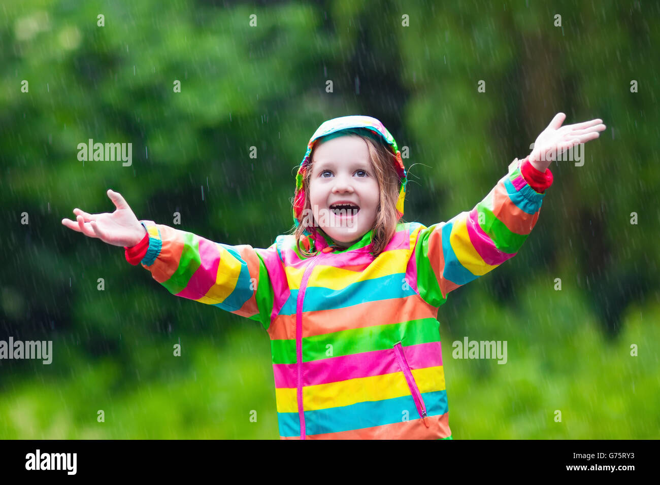 Little girl playing in rainy summer park. Child with colorful rainbow ...