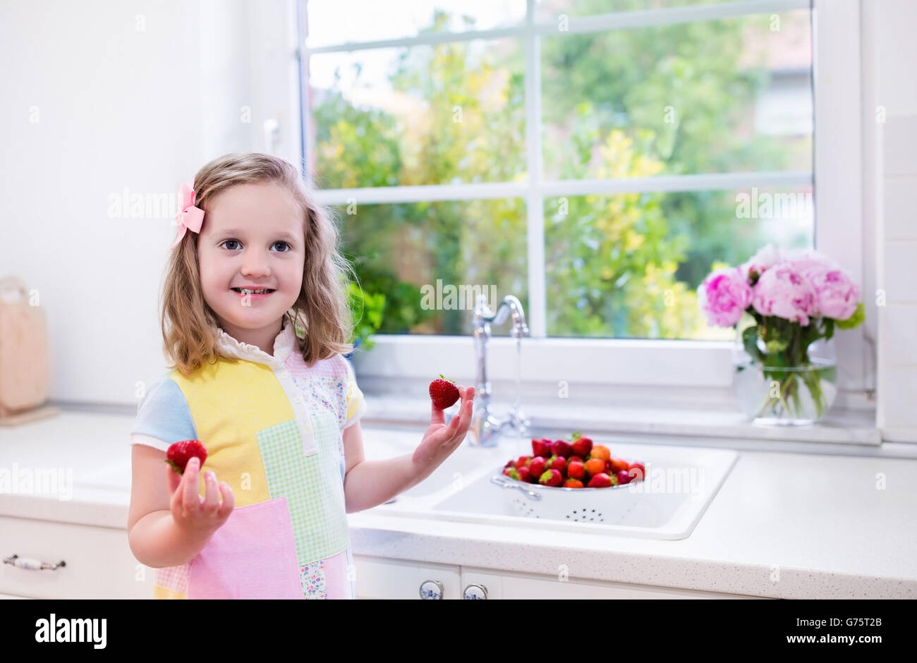 Cute little girl washing fruit in kitchen sink. Child eating strawberry ...