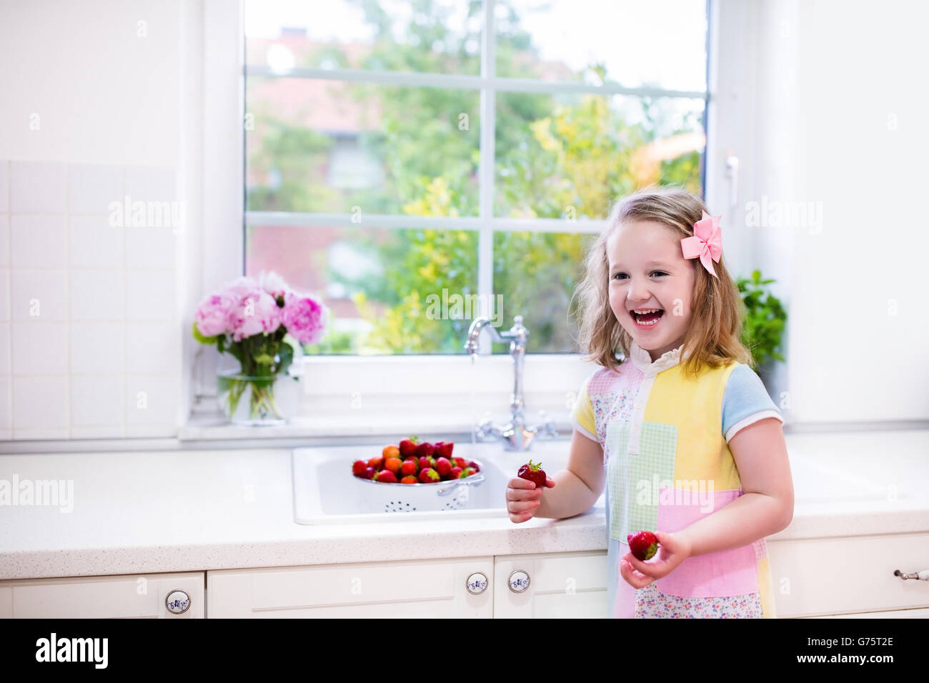 Cute little girl washing fruit in kitchen sink. Child eating strawberry ...