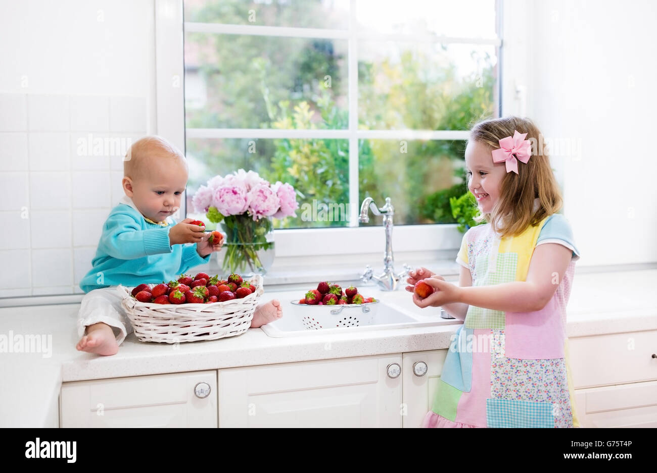 Cute little girl washing fruit in kitchen sink. Child eating strawberry ...
