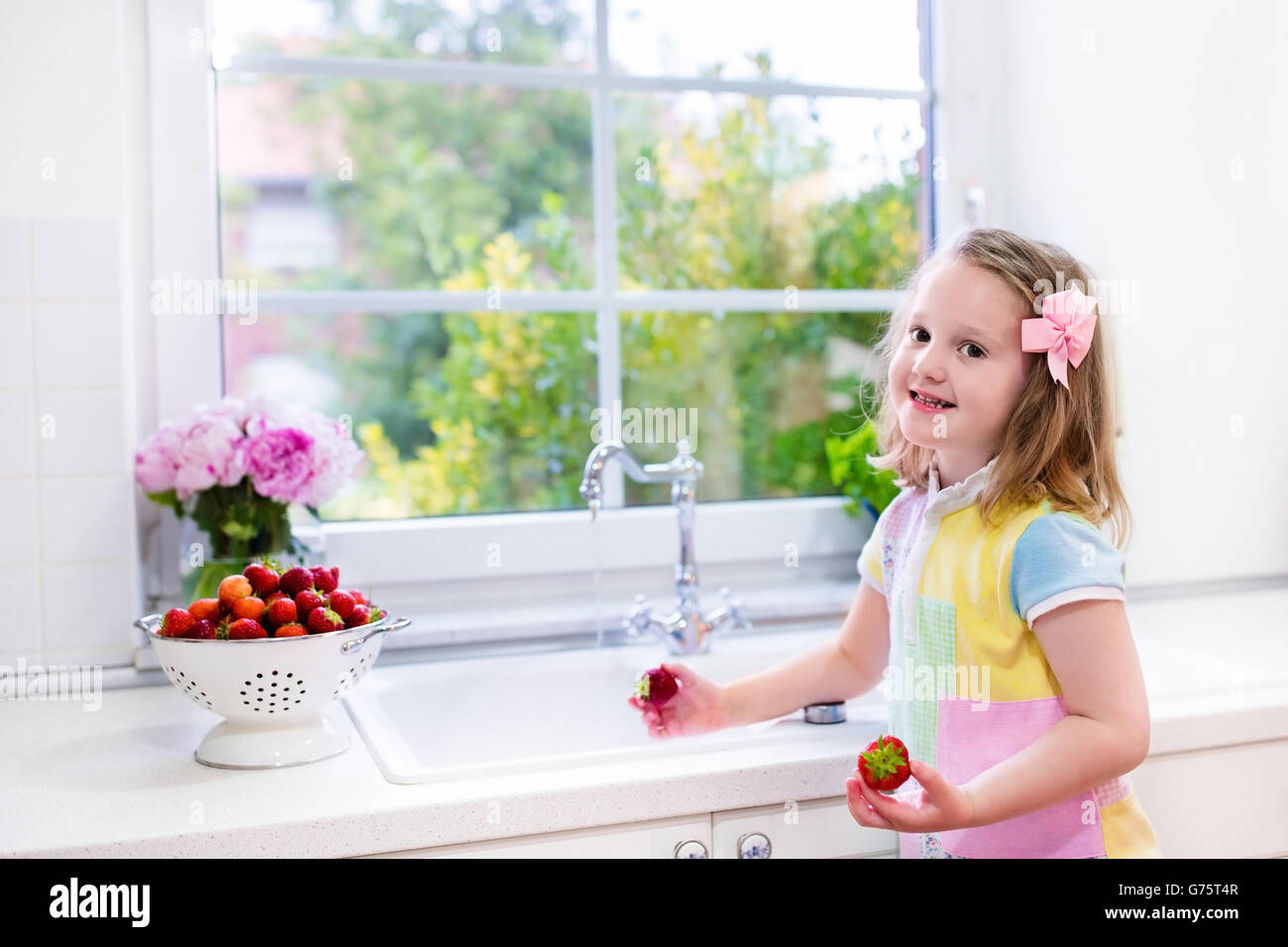 Cute little girl washing fruit in kitchen sink. Child eating strawberry ...