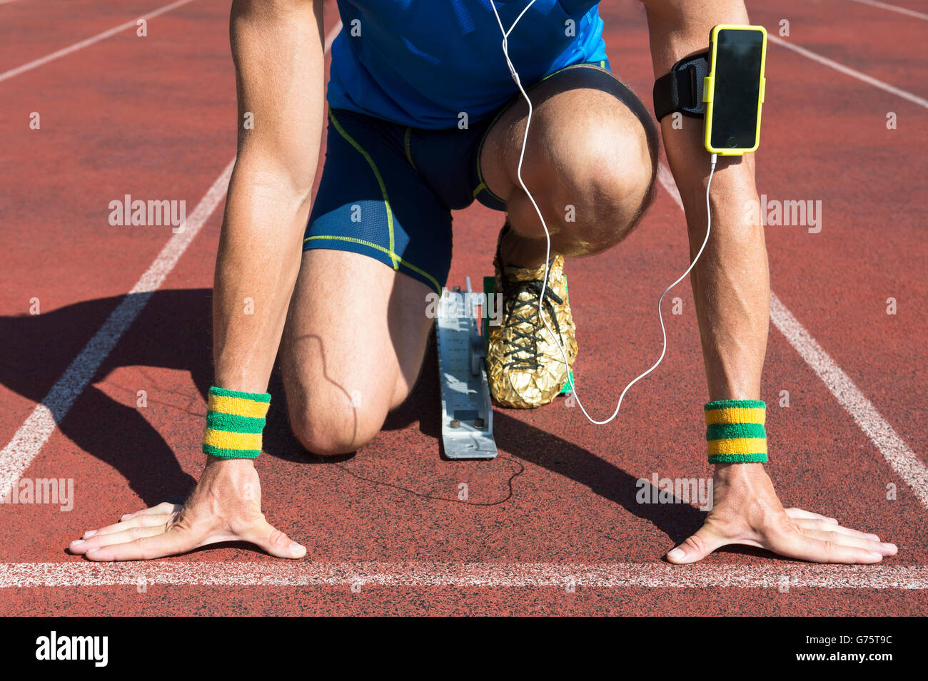 Athlete crouching at the starting line of a running track listening to ...