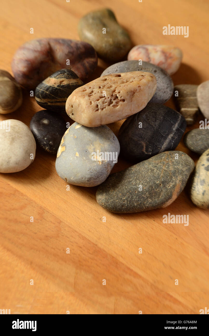 Rocks of various shapes and colors lying on light wood table. Grain of ...