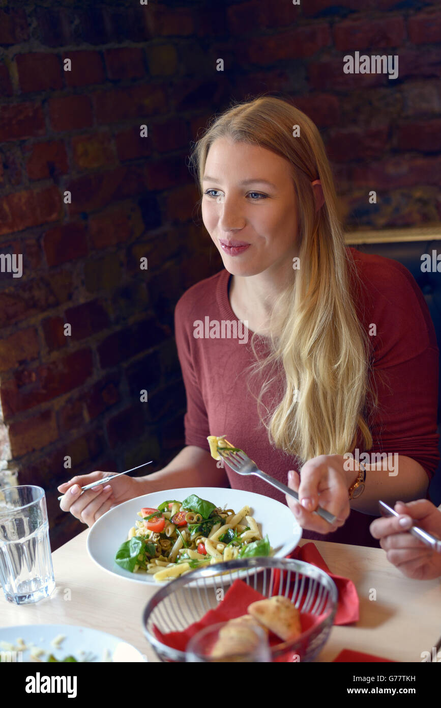 Smiling young woman in brown shirt and long blond hair eating a healthy ...