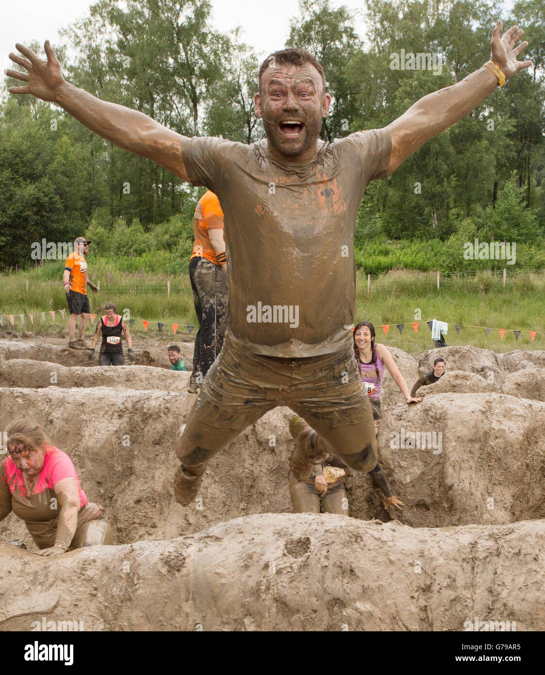 Having fun at Tough Mudders. Mud Mile obstacle, man jumping off mud ...