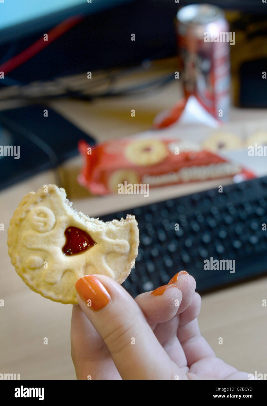 An office workers eats a Jammy Dodger biscuit at their desk, London ...