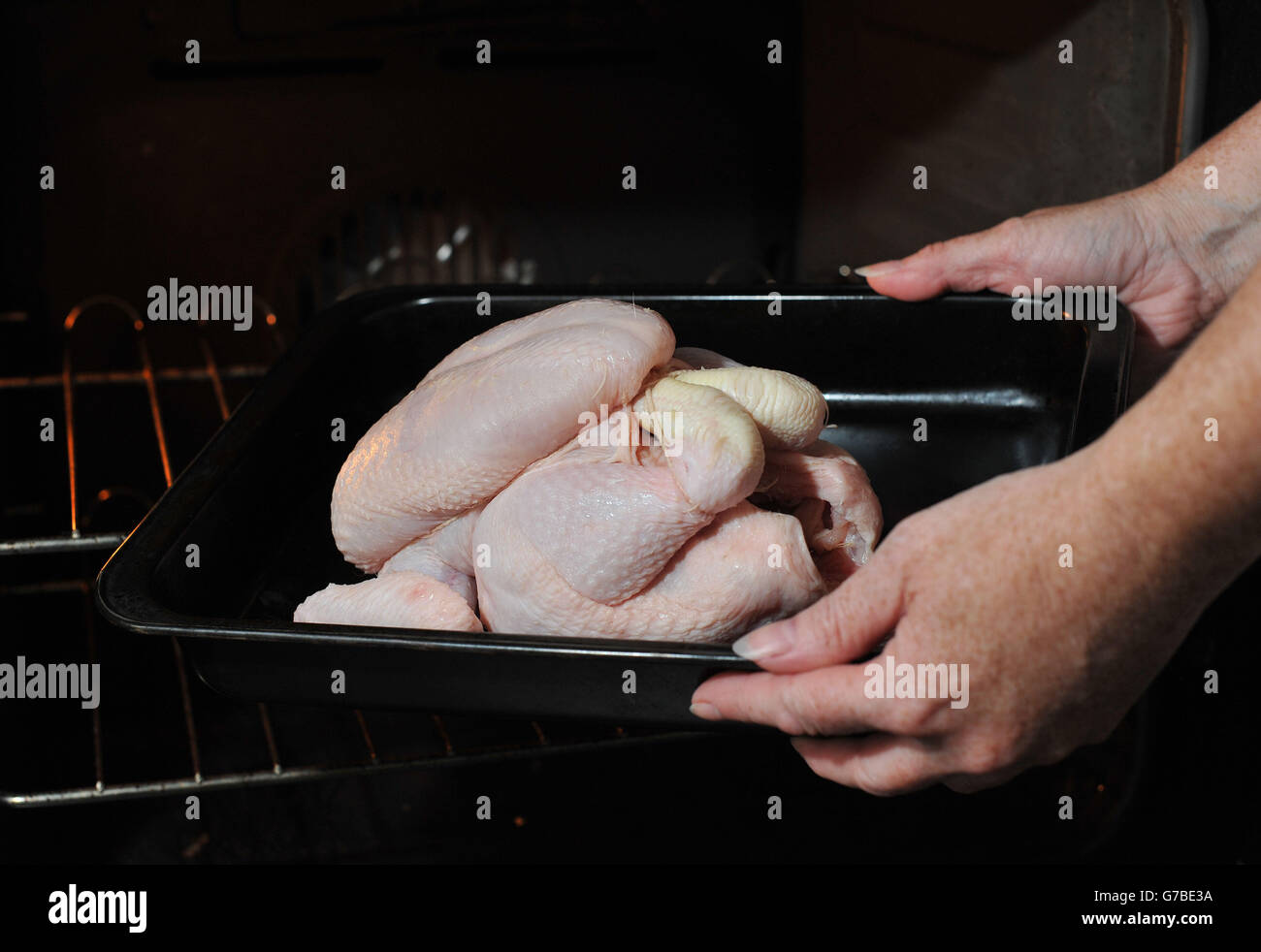 A raw chicken in a roasting tin being placed into an oven, as poor food ...