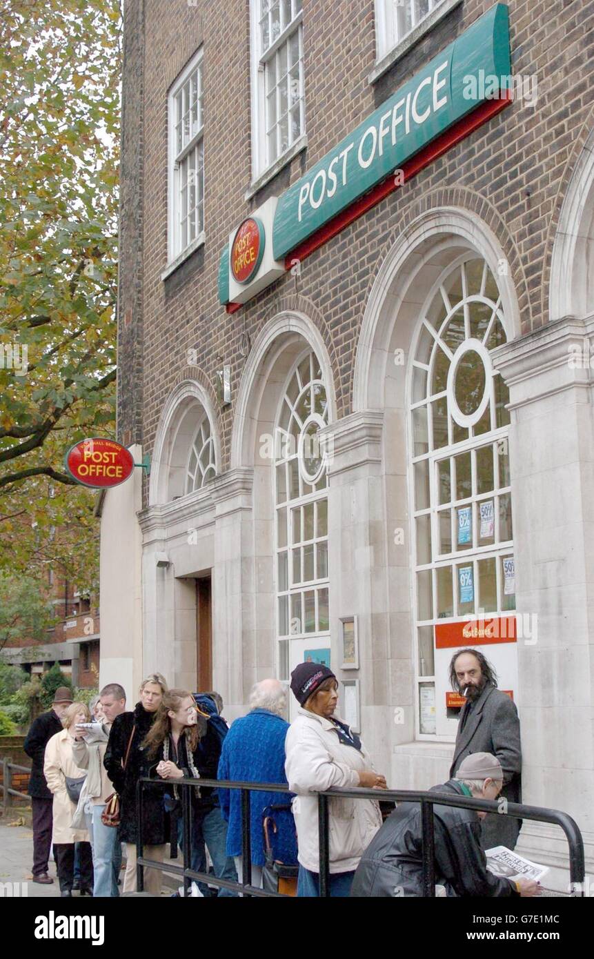 A queue of people builds up before opening-time outside a post office ...