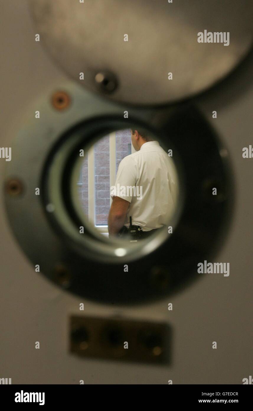 A Detention Custody Officer seen though a cell door observation hole at ...